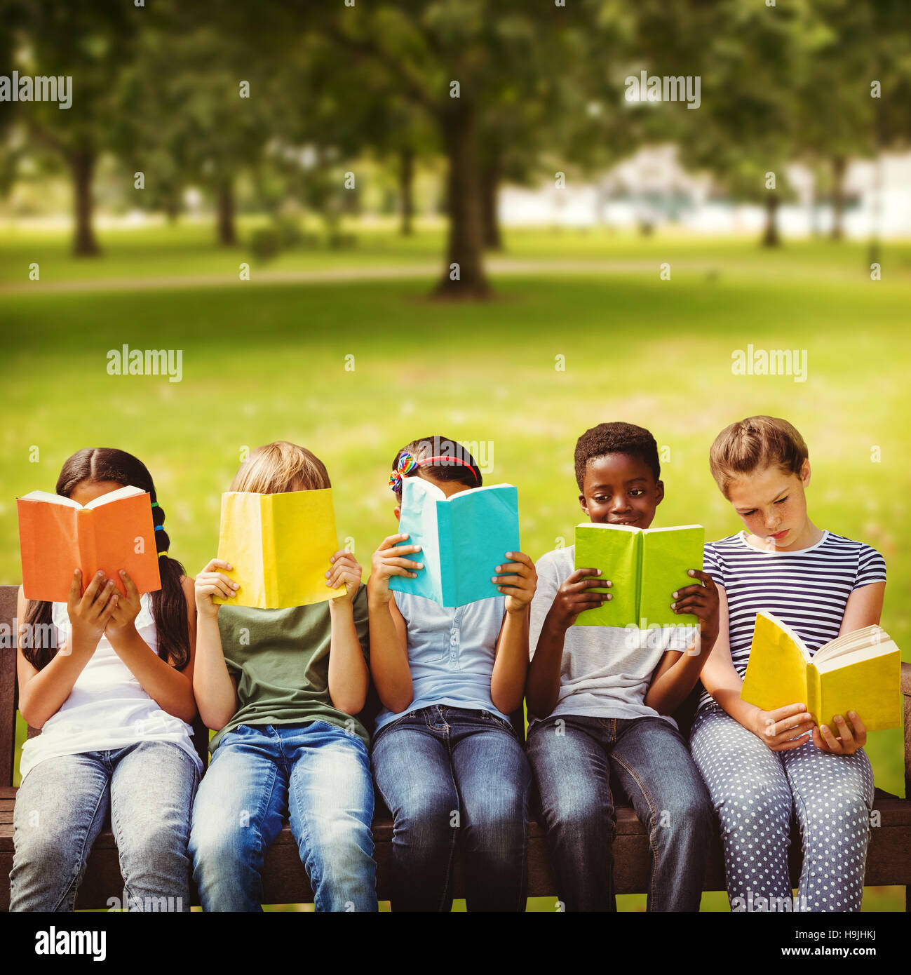 Composite image of children reading books at park Stock Photo - Alamy