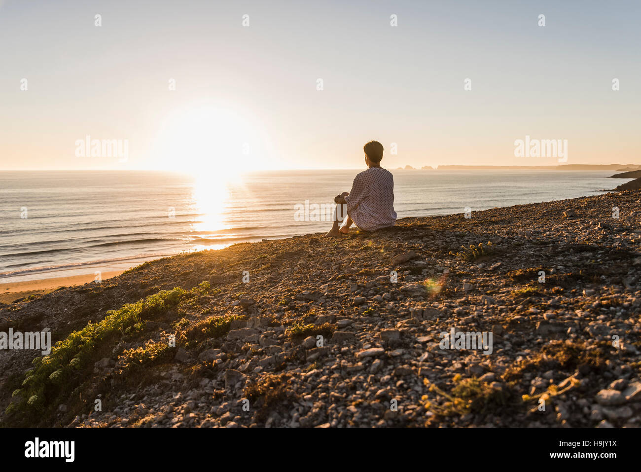 Back view of woman sitting on cliff watching sunset Stock Photo - Alamy