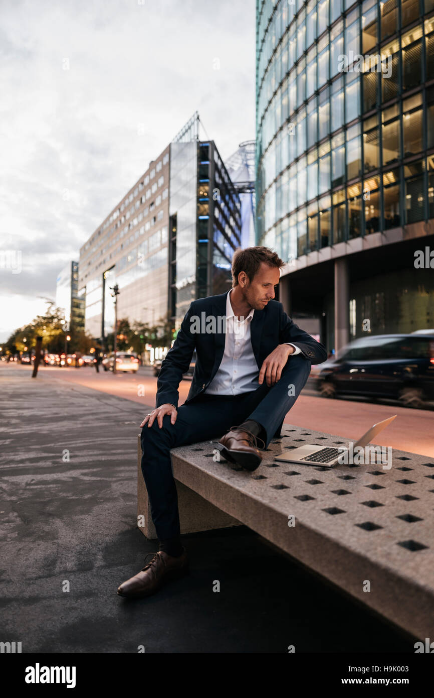 Germany, Berlin, Potsdamer Platz, businessman sitting on bench using ...