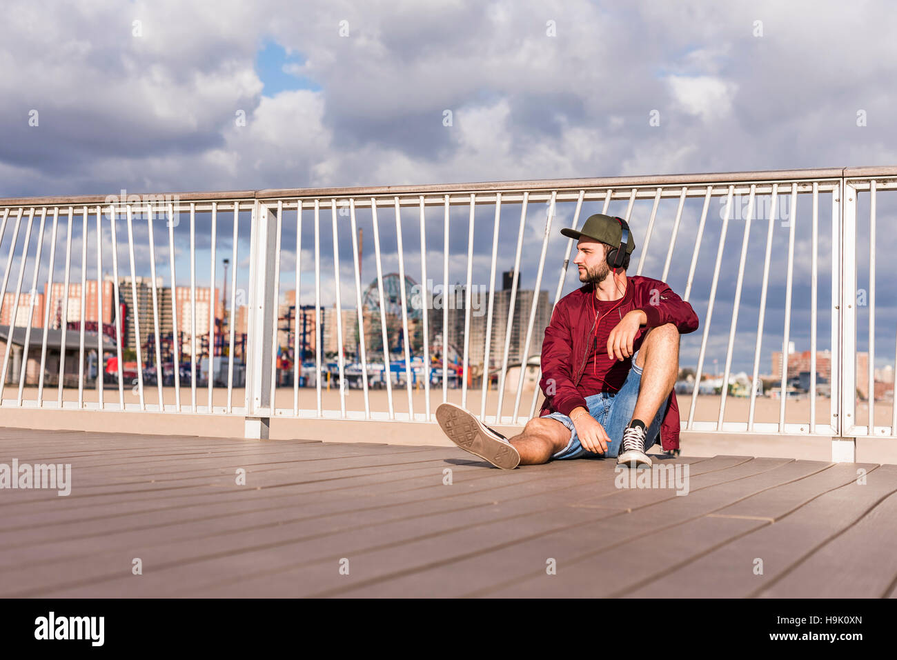 USA, New York City, man sitting on bridge on Coney Island wearing ...