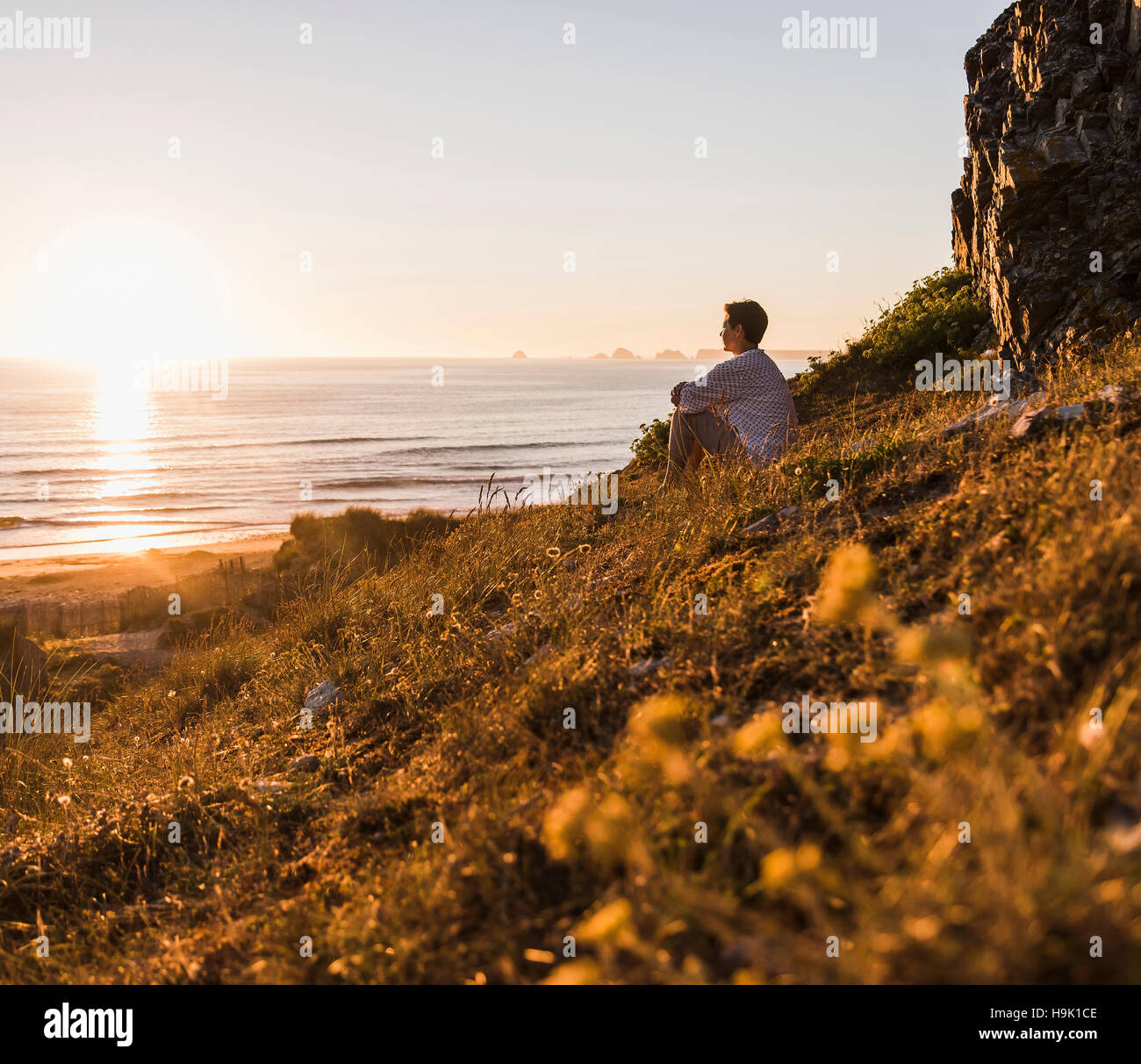 Woman sitting on cliff watching sunset Stock Photo - Alamy