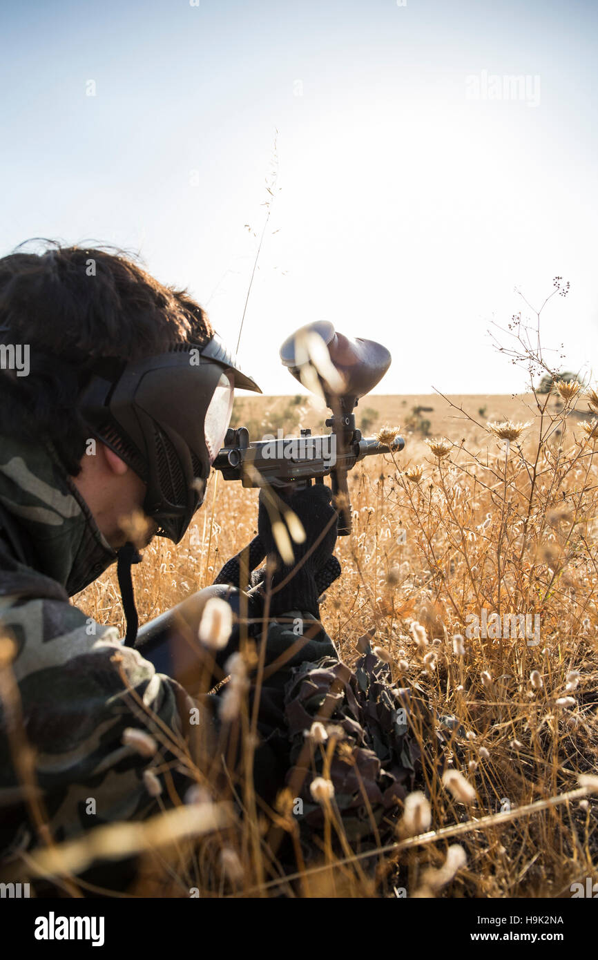 Paintball player lying in grass aiming with paintball gun during a ...