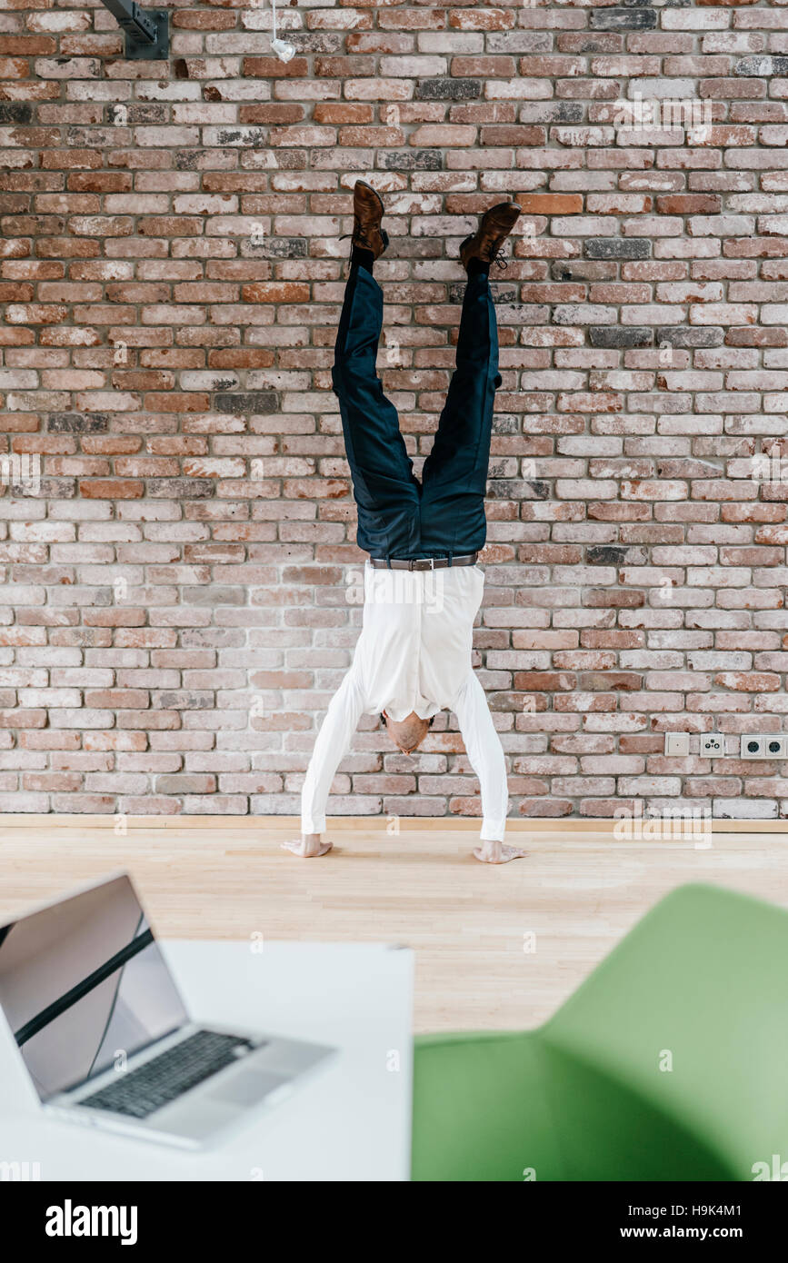 Businessman doing a handstand in front of brick wall Stock Photo - Alamy