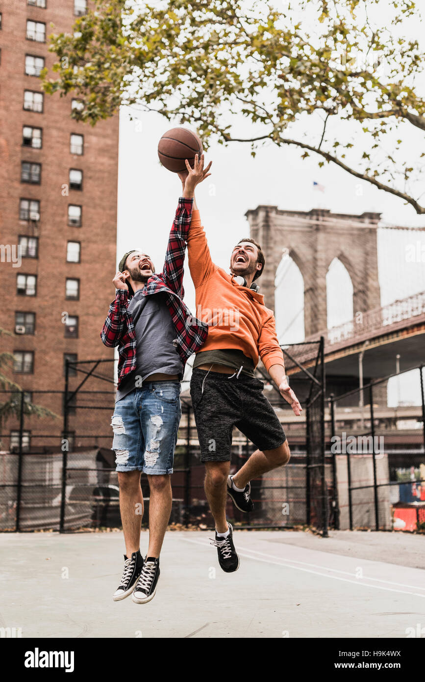 USA, New York, two young men playing basketball on an outdoor court ...