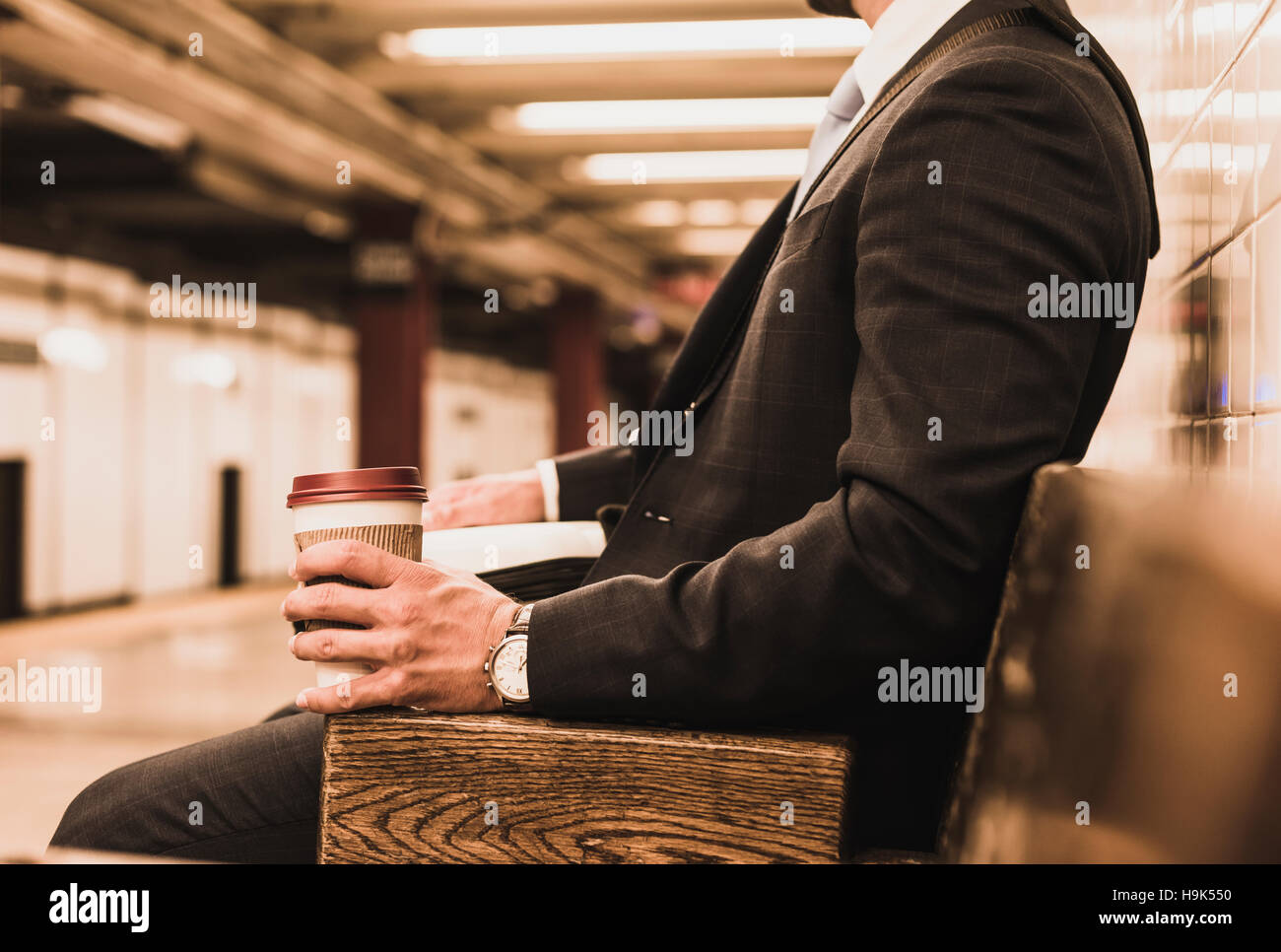 Young businessman waiting at metro station platform, holding disposable ...