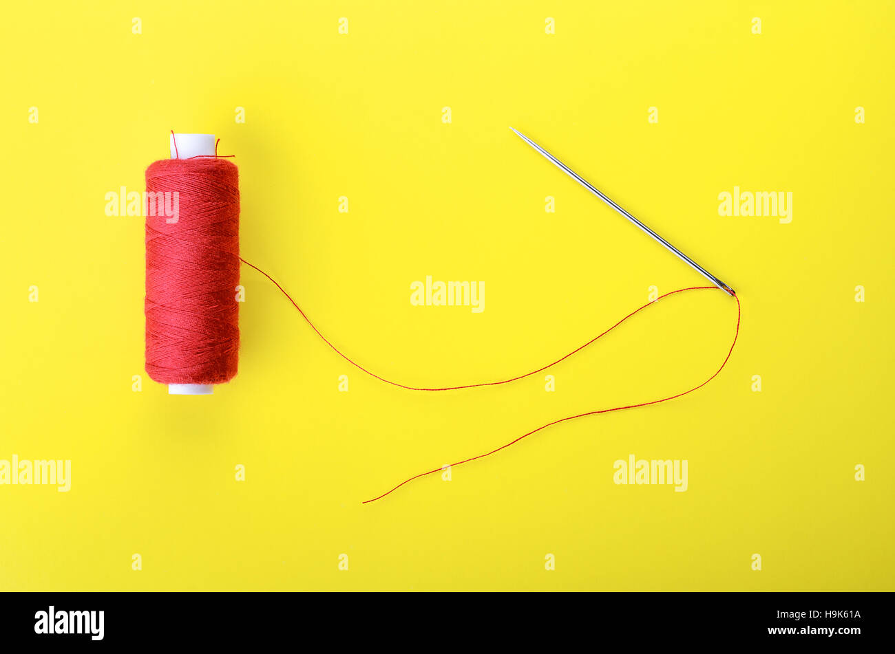 Spool of red thread and needle on yellow background, symbol of handmade ...