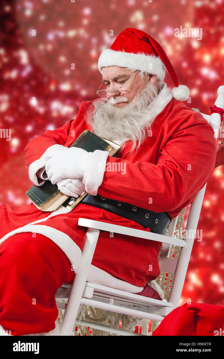 Composite image of santa claus holding bible while relaxing on chair ...