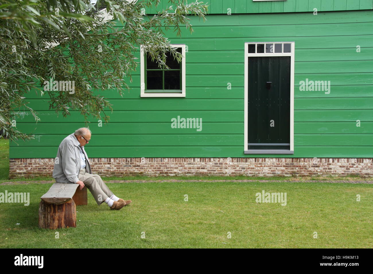 Lonely old man sits on a bench under a tree outside his home image in ...
