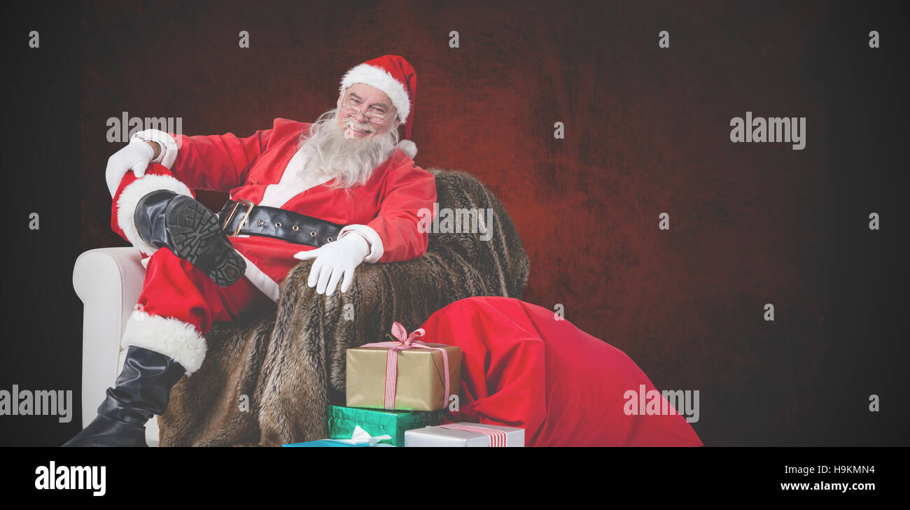Composite image of portrait of santa sitting on sofa with sack of ...