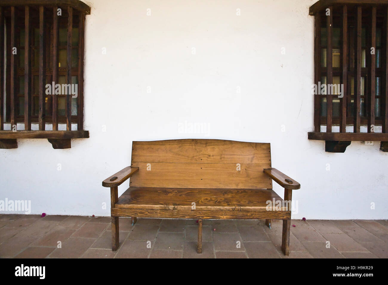 Vintage wooden bench on covered portico between wooden-barred windows ...