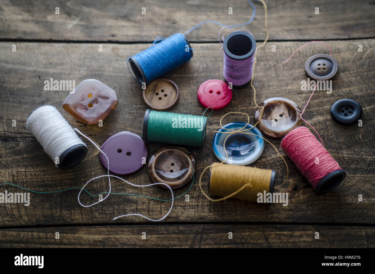Bobbins with colorful threads and buttons on old wooden table ...