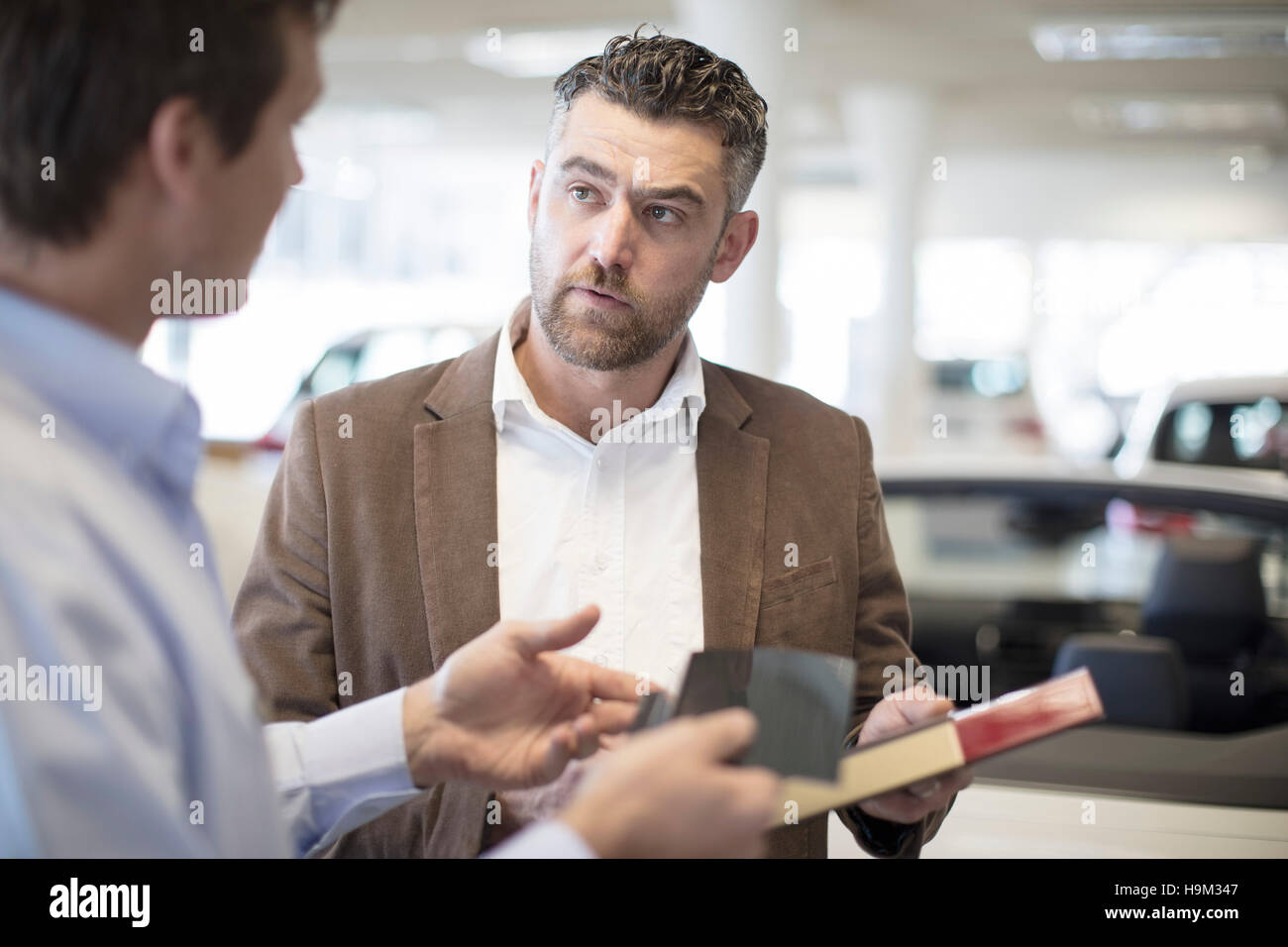 Car dealer handing over color sample to client in showroom Stock Photo ...