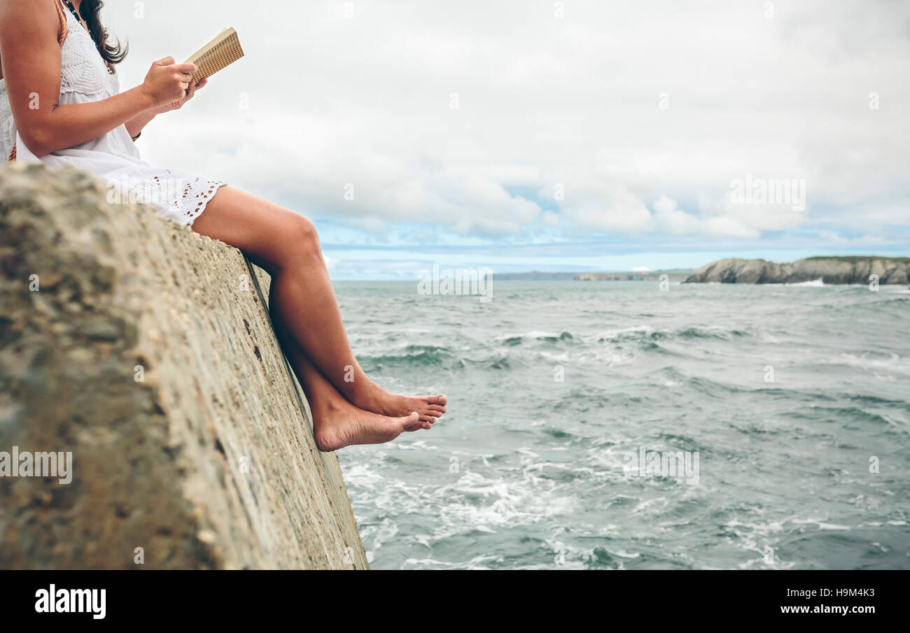 Barefoot woman sitting on pier reading a book, partial view Stock Photo ...