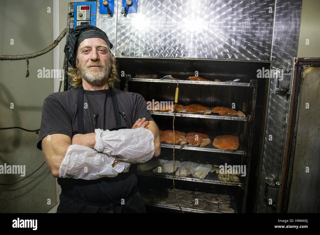 Proud smokehouse owner standing in front of smoker full of fish Stock ...