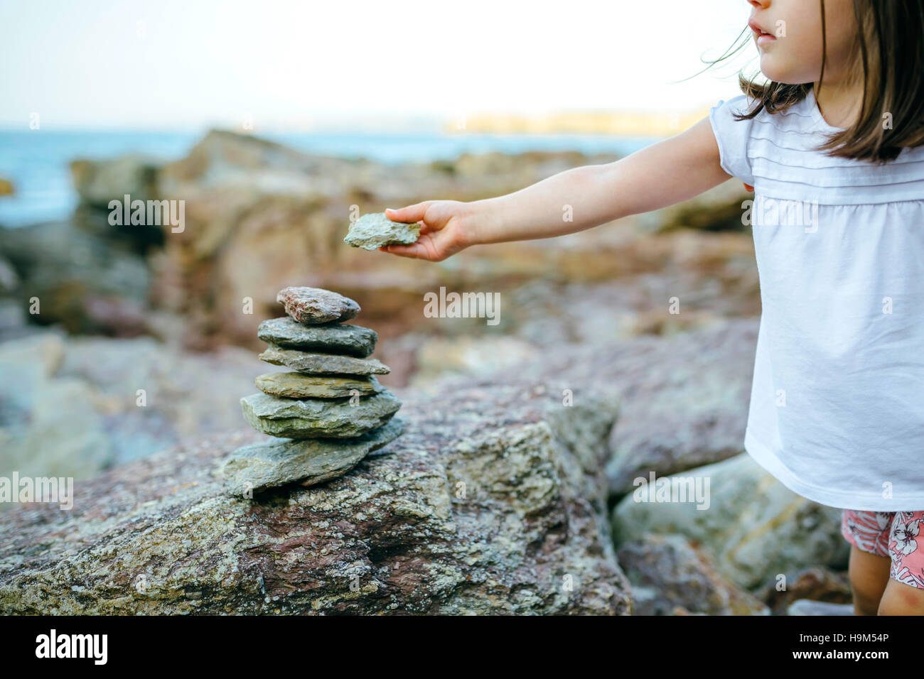 Girl stacking stones at rocky coast Stock Photo - Alamy