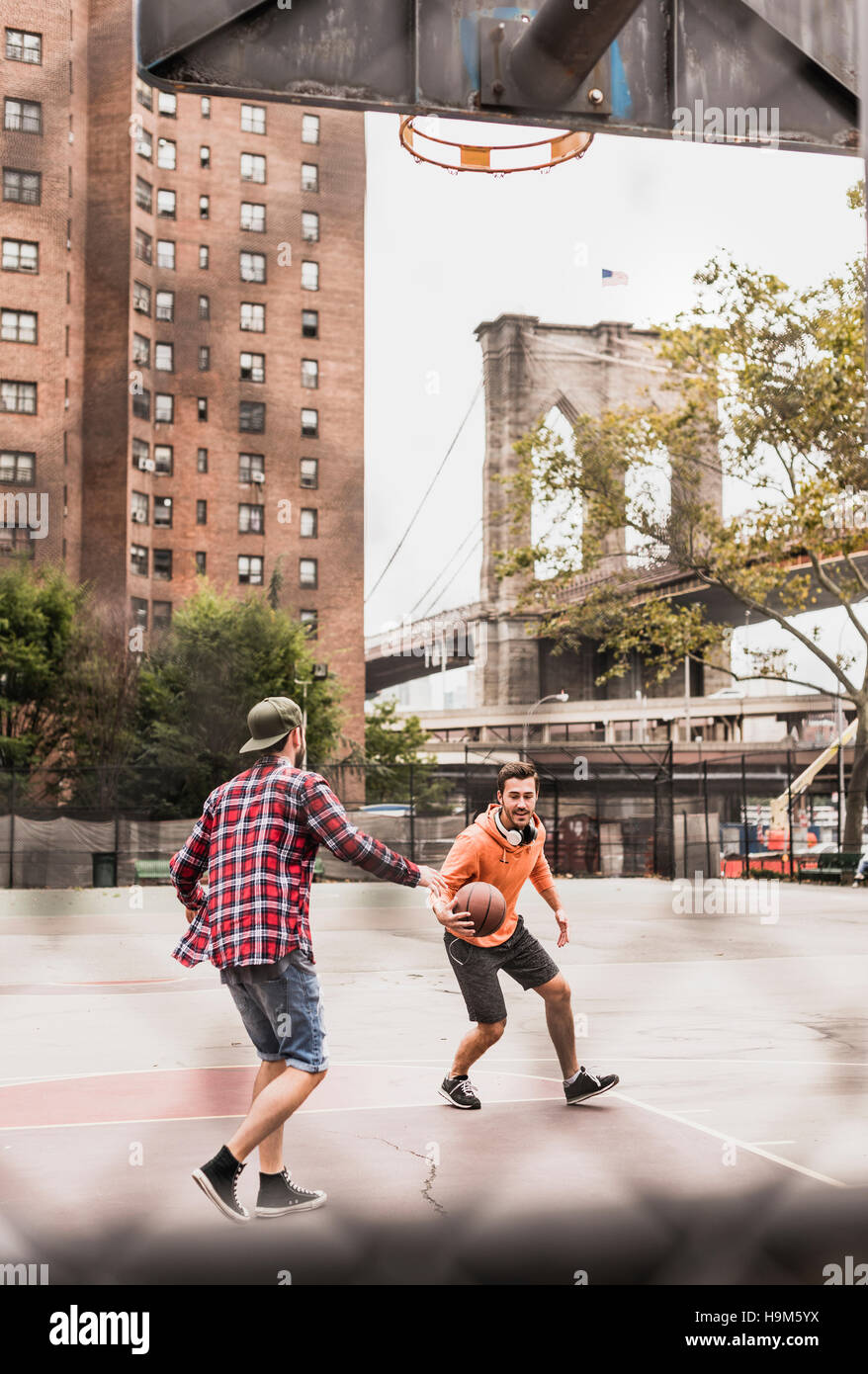 USA, New York, two young men playing basketball on an outdoor court ...