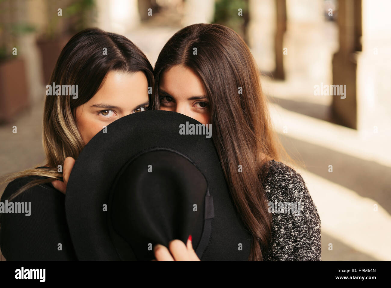 Two best friends hiding their mouths behind black hat Stock Photo - Alamy
