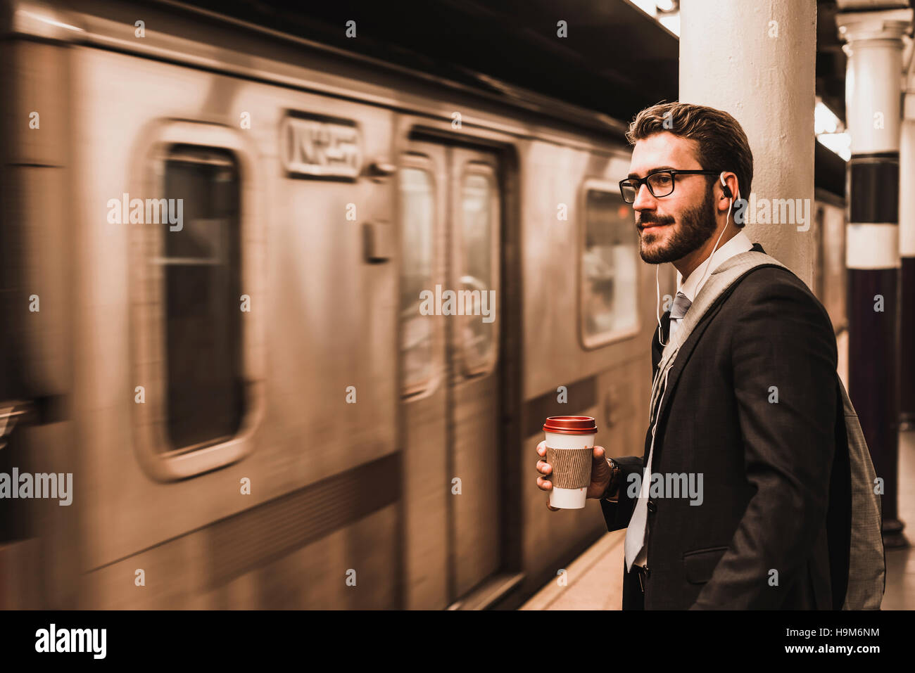 Young businessman waiting at metro station platform, holding disposable ...