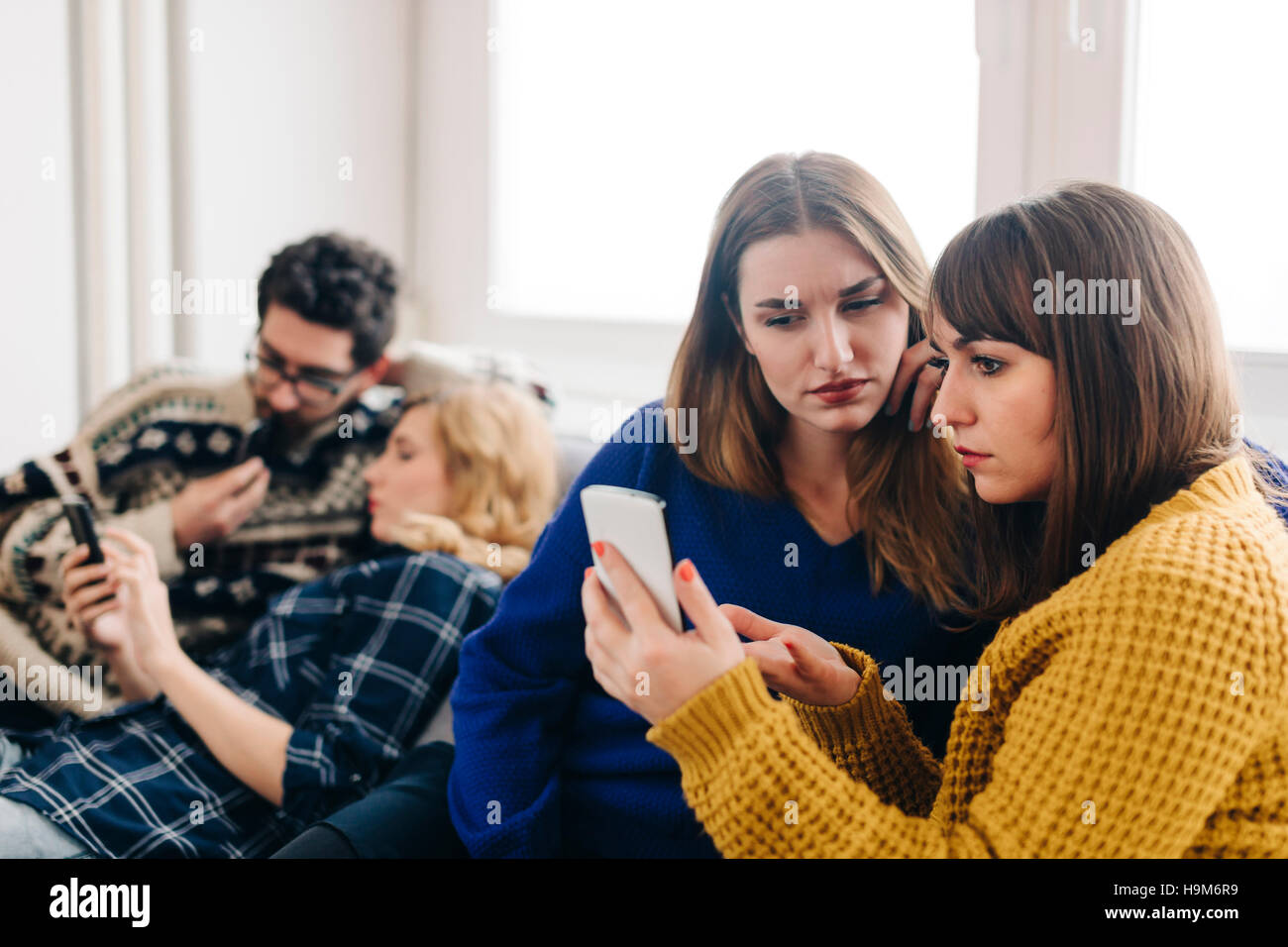 Young woman sharing message on smartphone with friend in living room ...