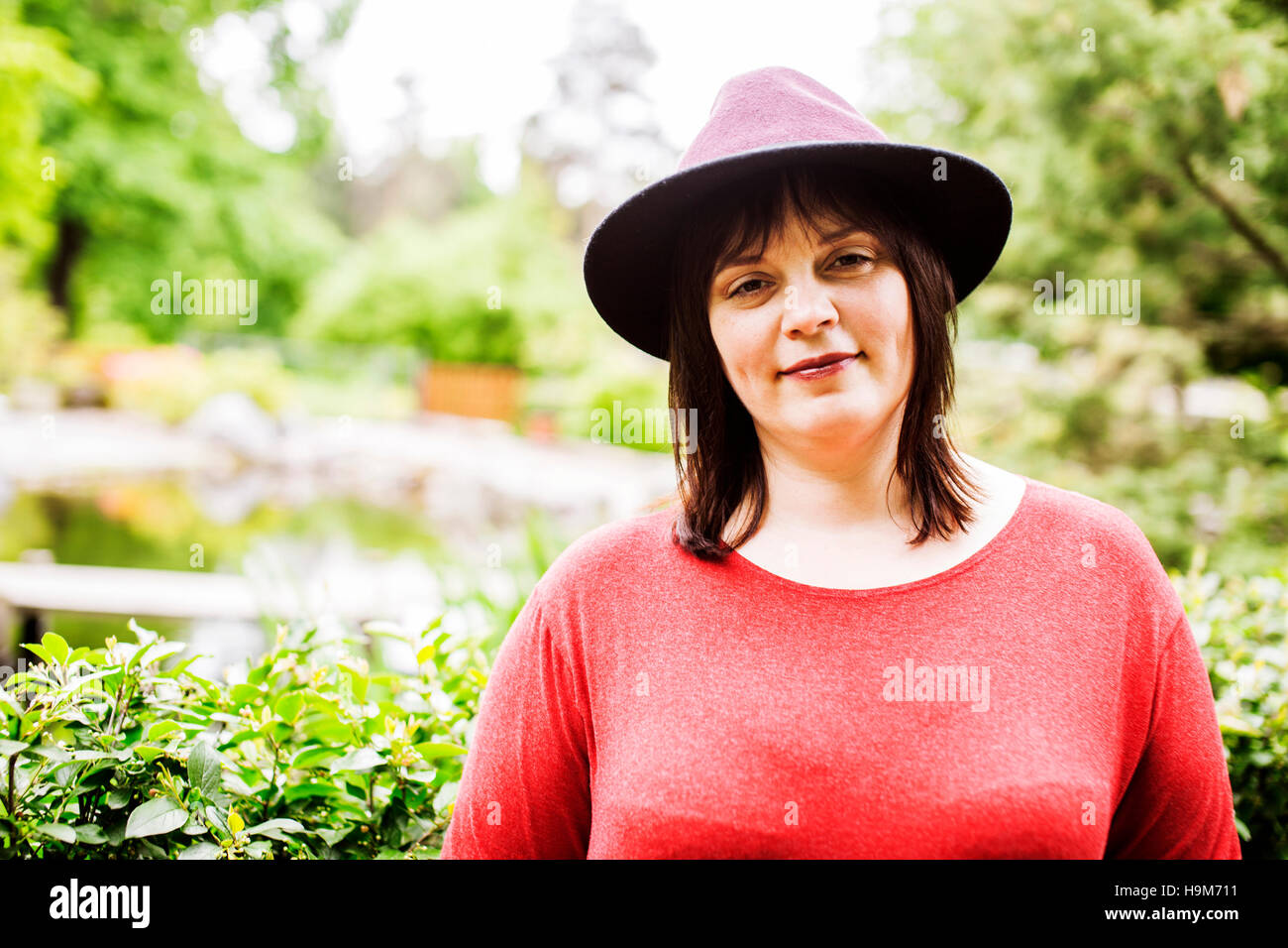mature brunette woman in green garden wearing hat, smiling, frie Stock ...