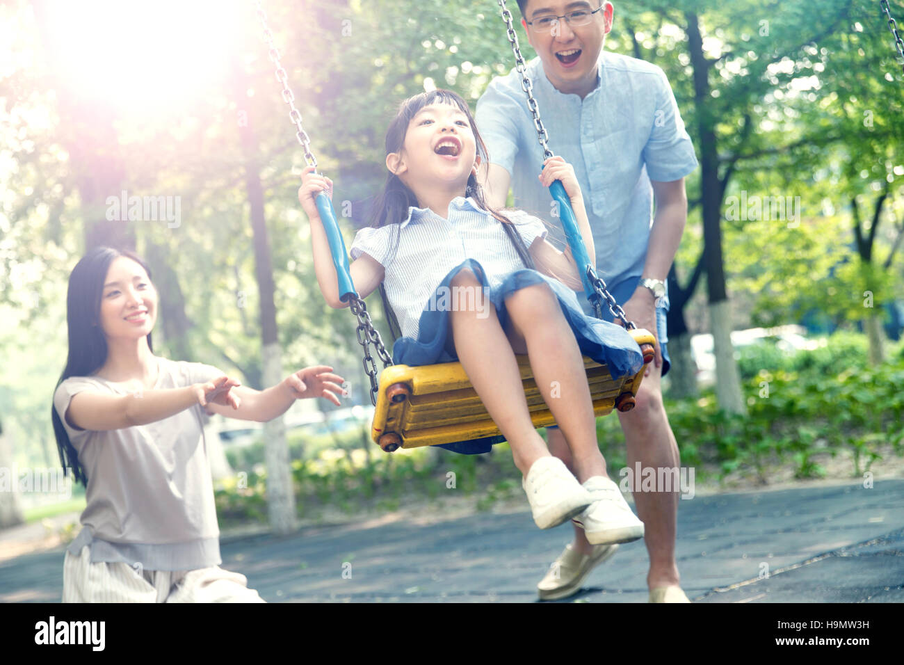 Happy family of three swing Stock Photo - Alamy
