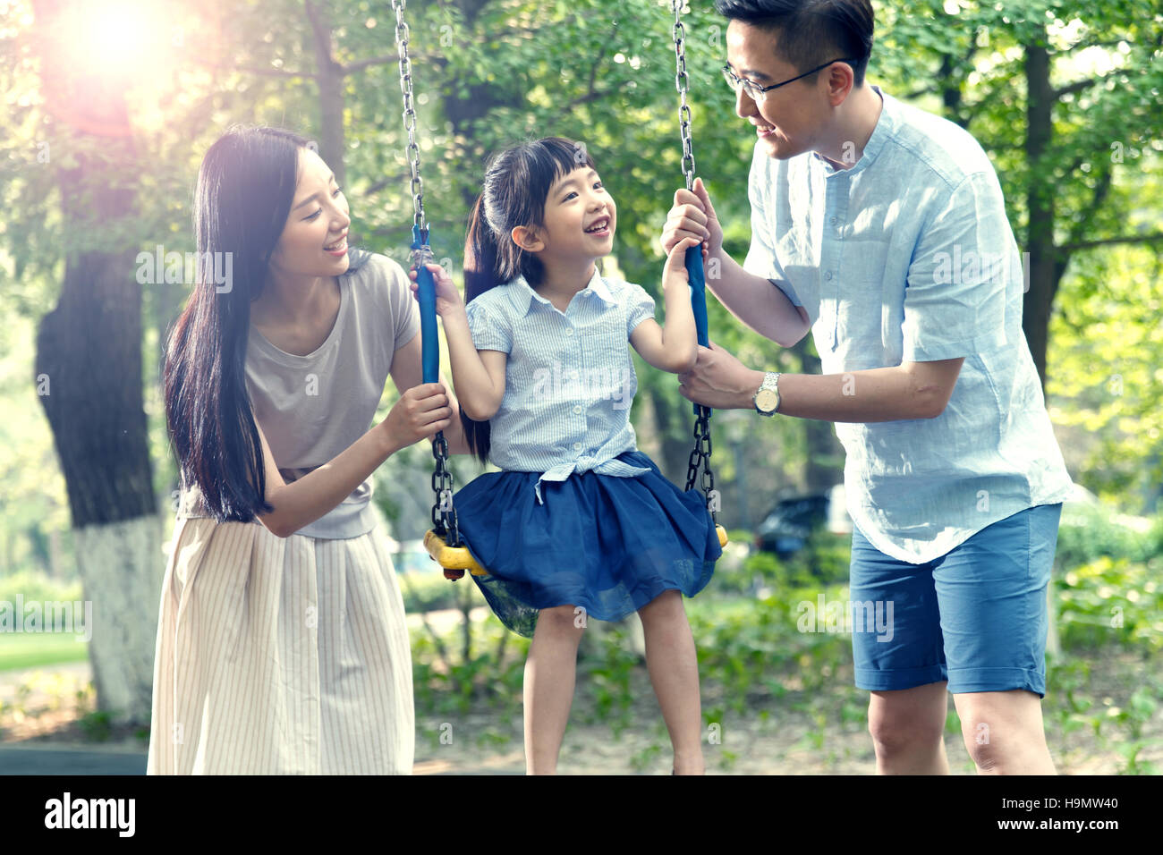 Happy family of three swing Stock Photo - Alamy