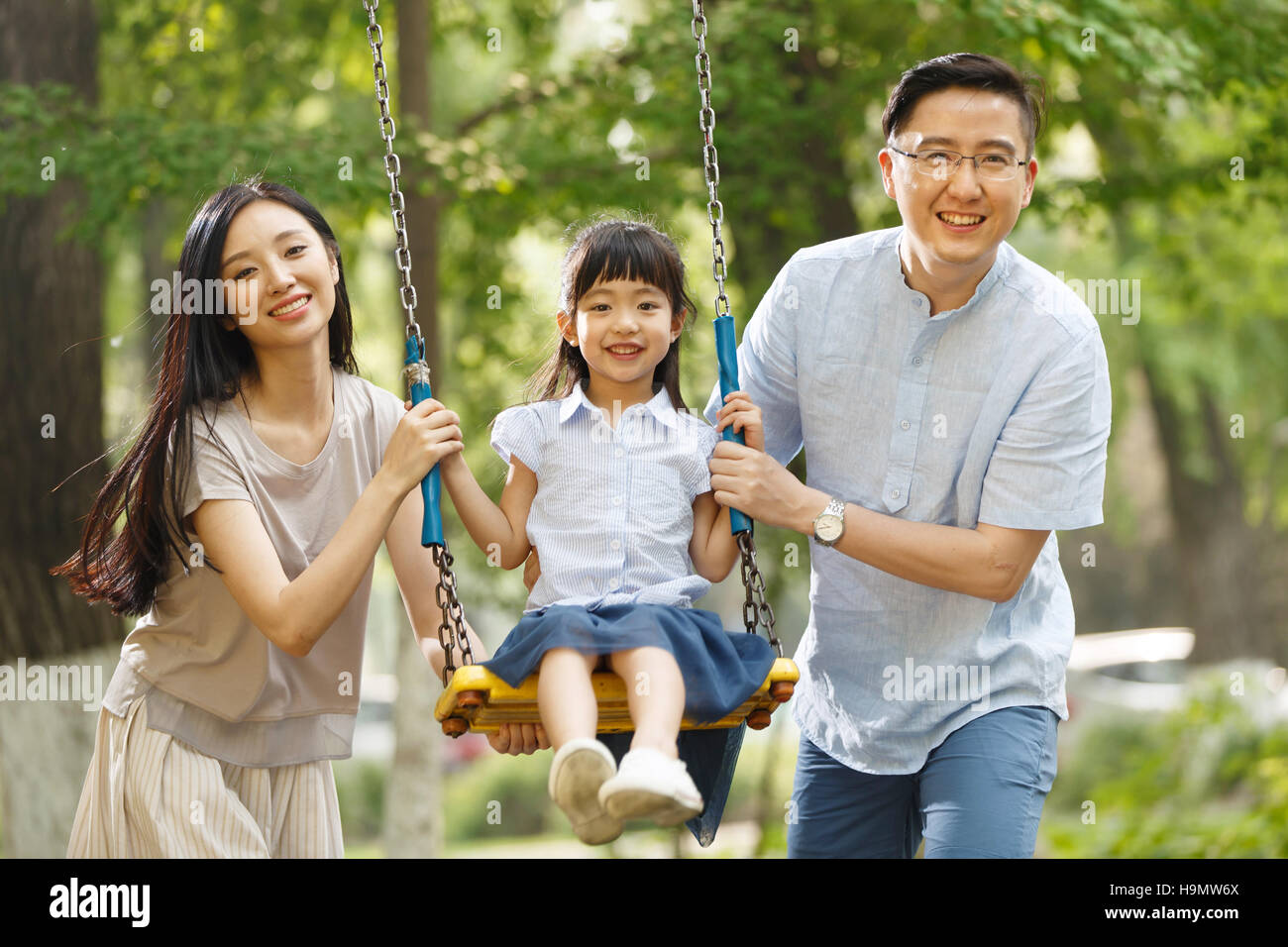 Happy family of three swing Stock Photo - Alamy
