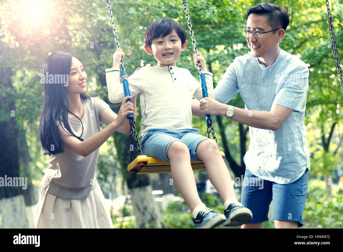 Happy family of three swing Stock Photo - Alamy