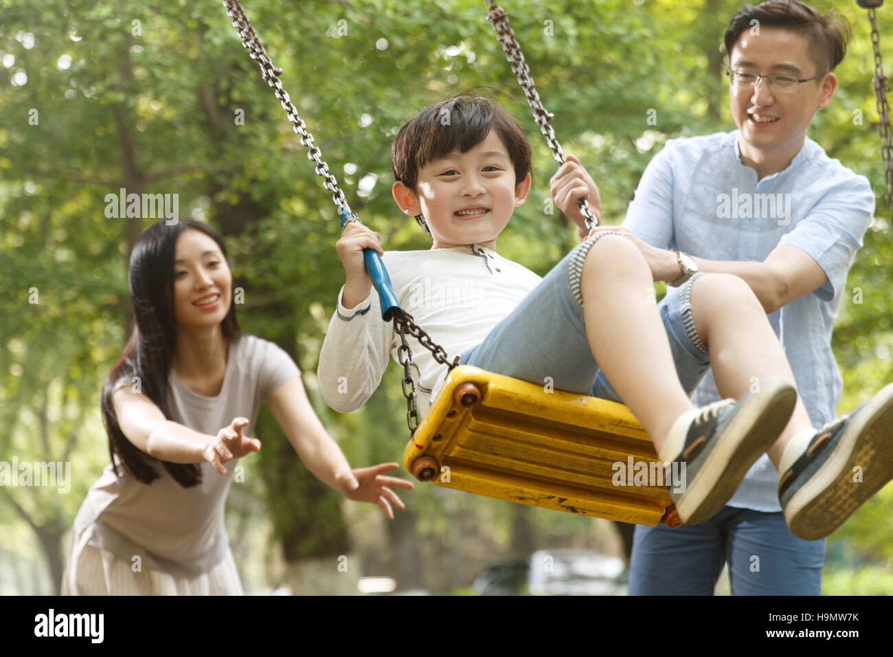 Happy family of three swing Stock Photo - Alamy