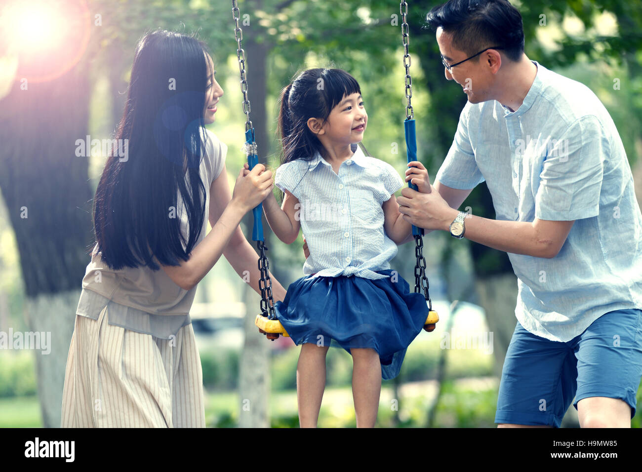 Happy family of three swing Stock Photo - Alamy