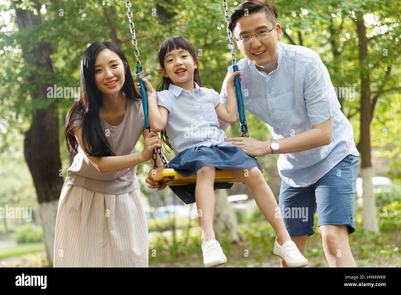 Happy family of three swing Stock Photo - Alamy