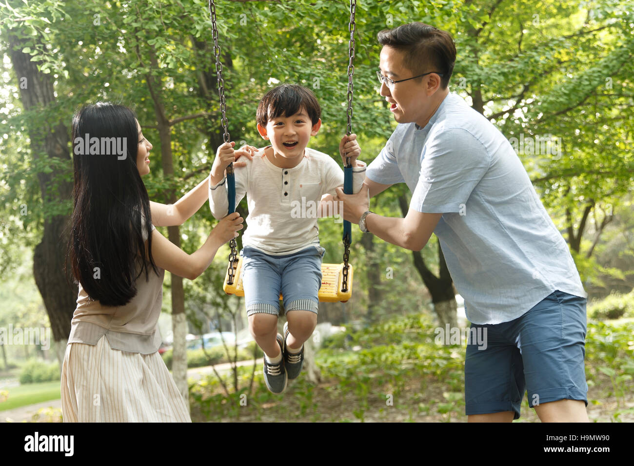 Happy family of three swing Stock Photo - Alamy