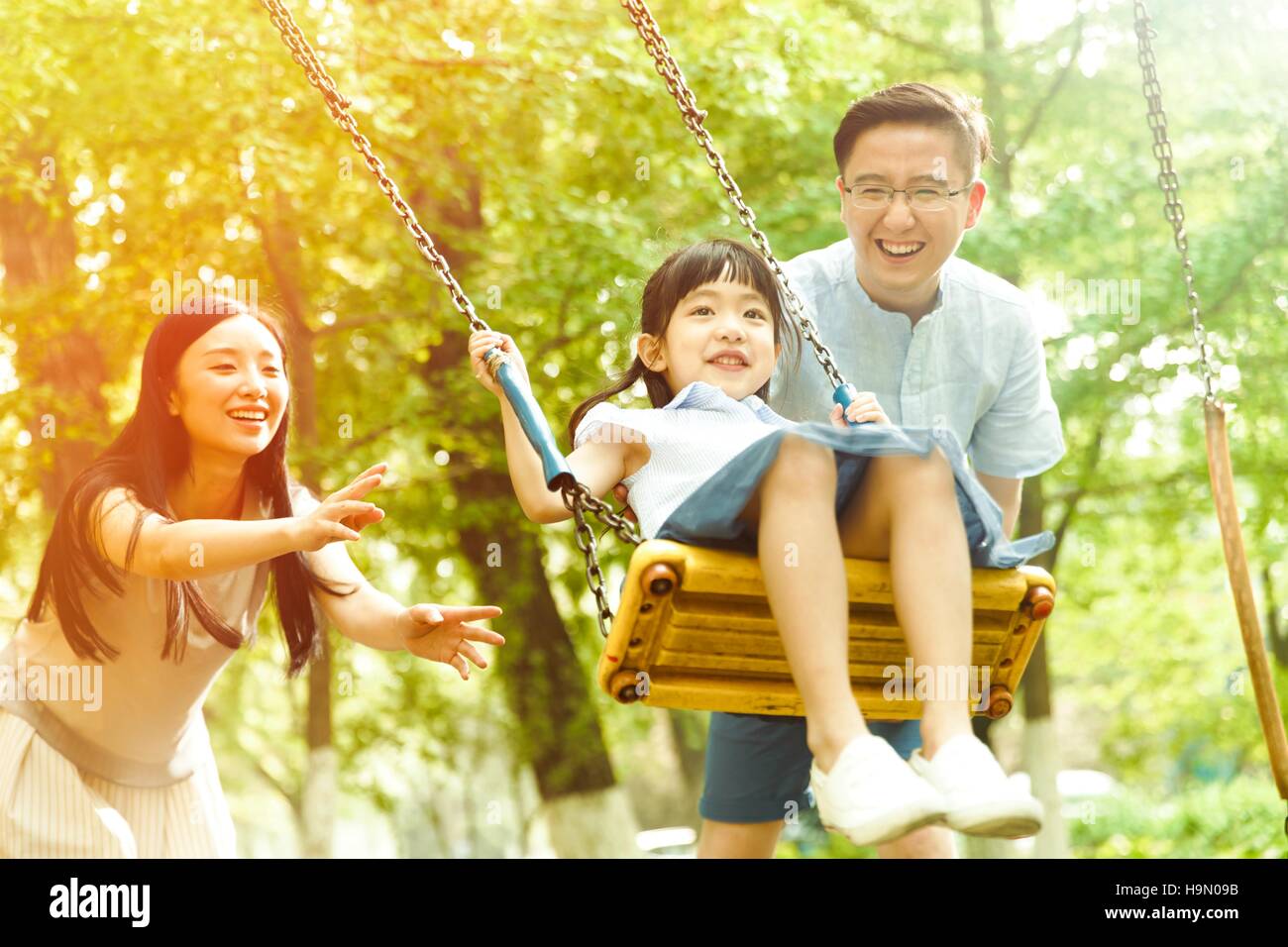 Happy family of three swing Stock Photo - Alamy
