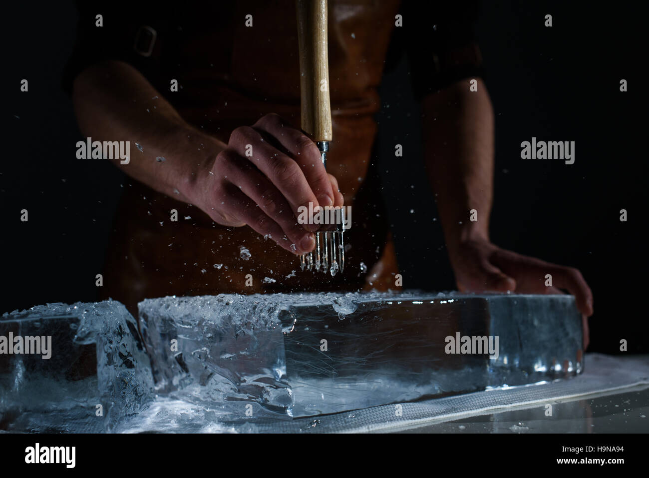 Bartender chopping ice using a special knife. Peaces of ice goes around ...