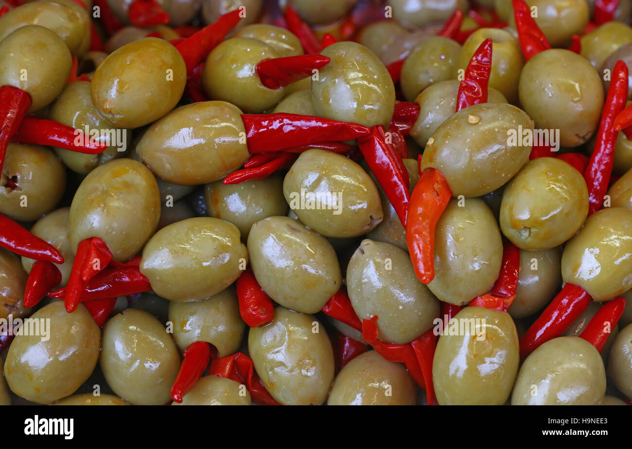 Green pitted olives stuffed with red hot chili peppers in oil close up ...