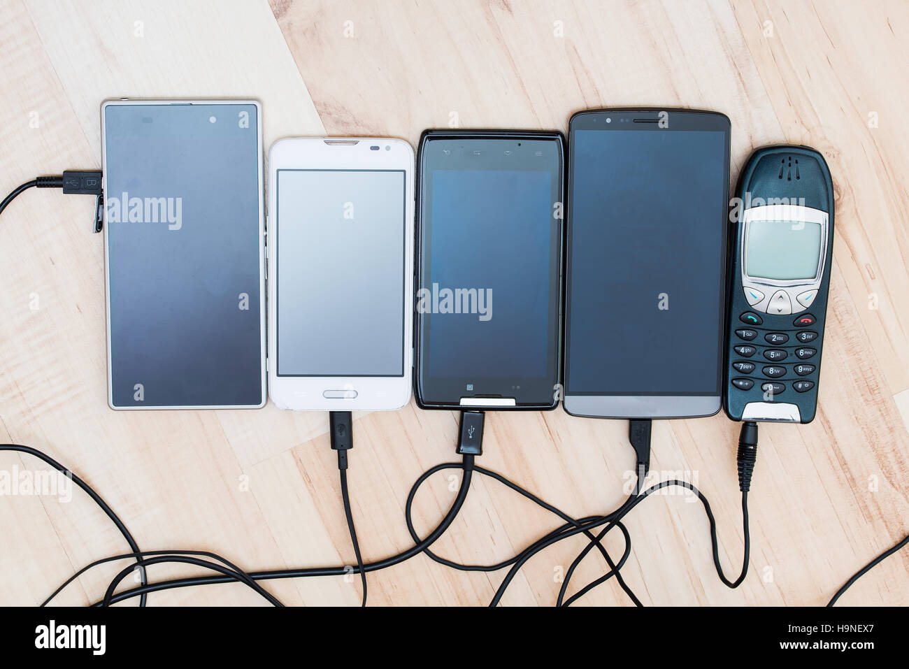 four smartphones and one classic phone connected to chargers Stock ...