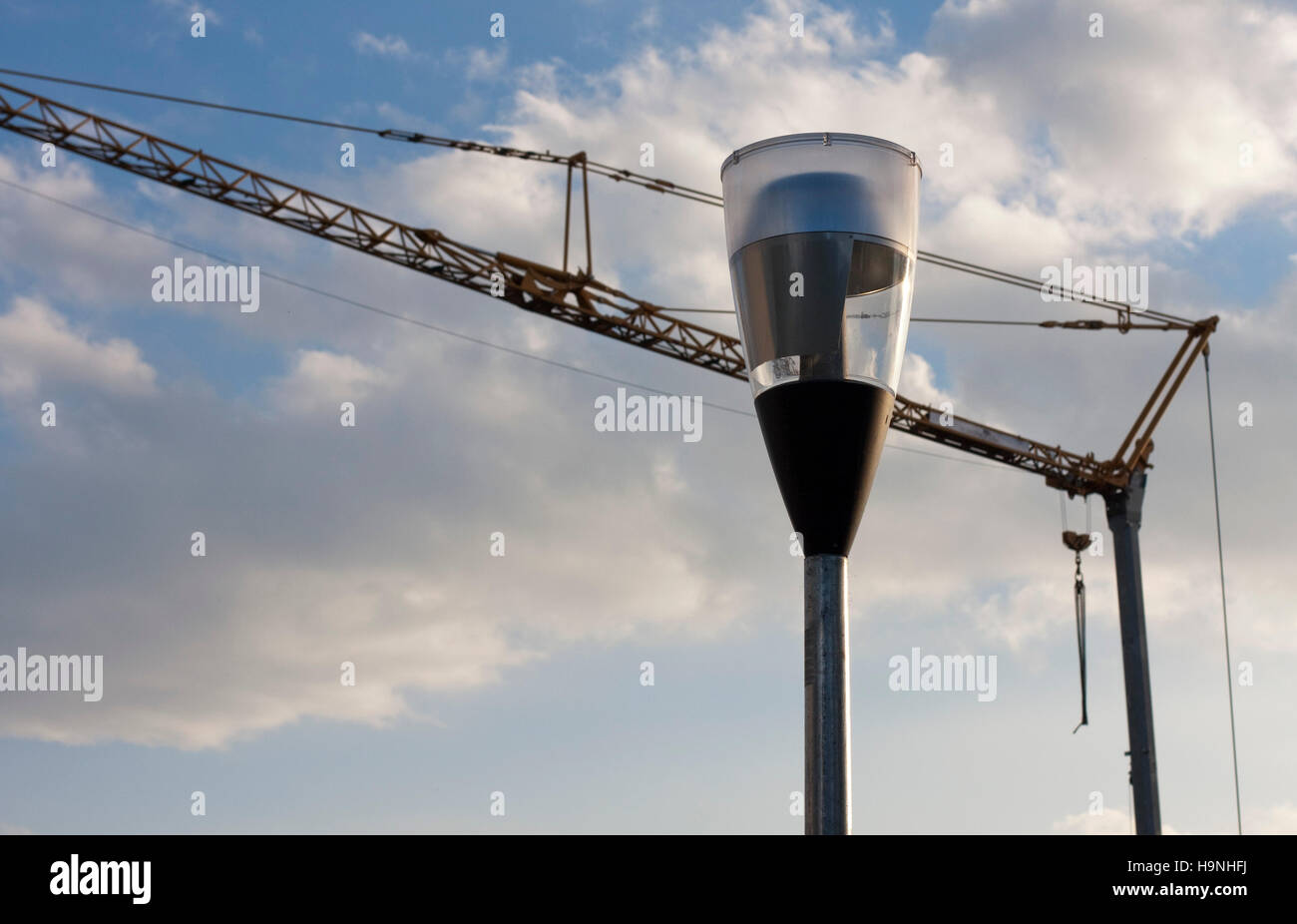 Stylish modern street light against construction crane, clouds and blue ...