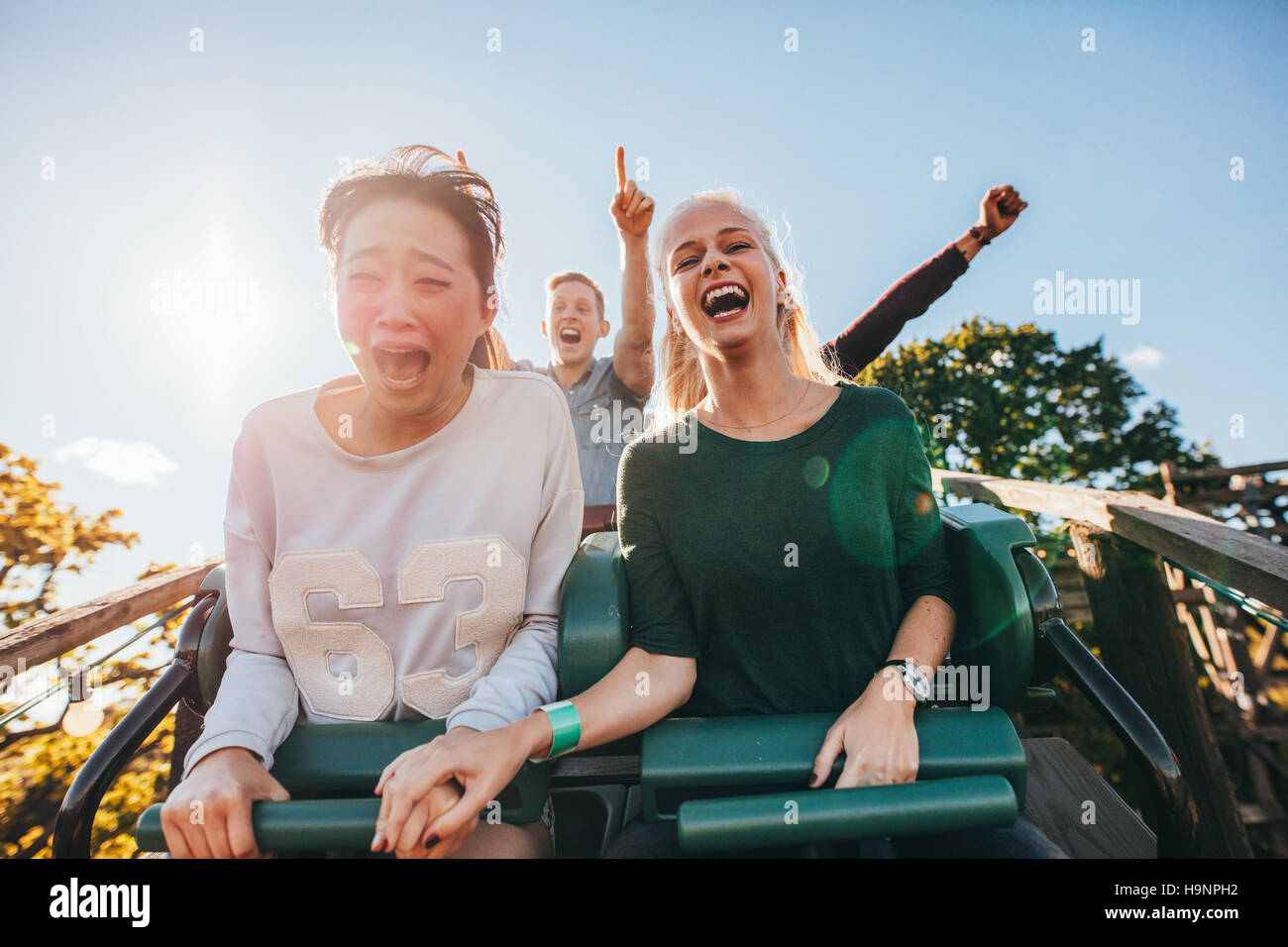 Enthusiastic young friends riding roller coaster ride at amusement park ...