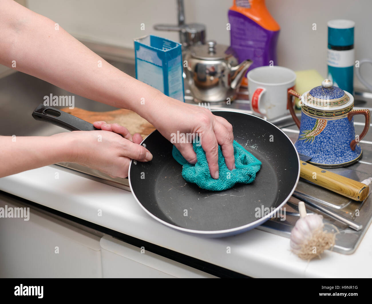 Houseproud woman washing a frying pan in her messy kitchen, cropped ...