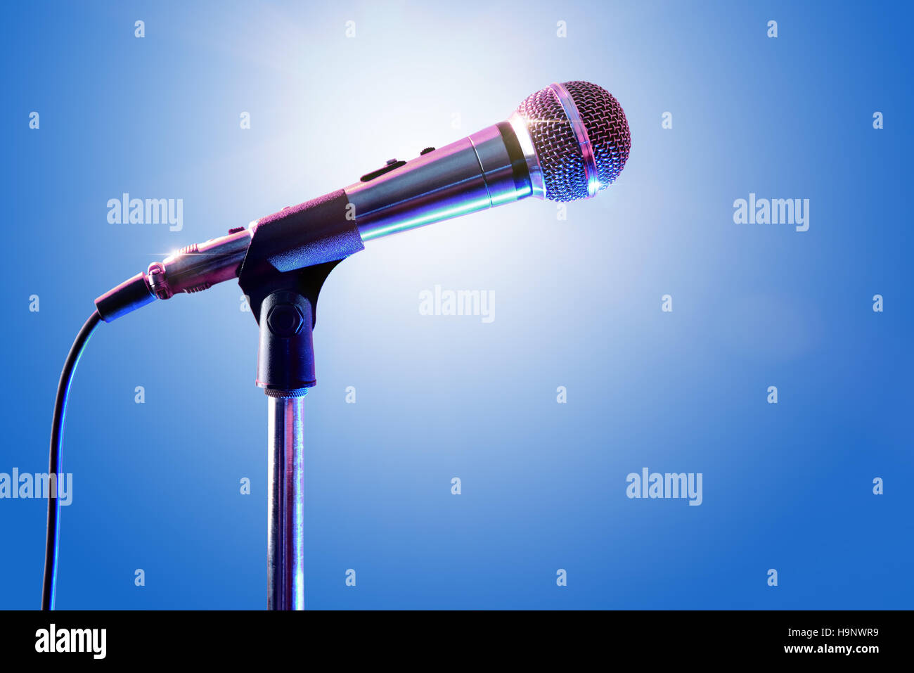 Microphone on microphone stand with cable and blue background. Front ...