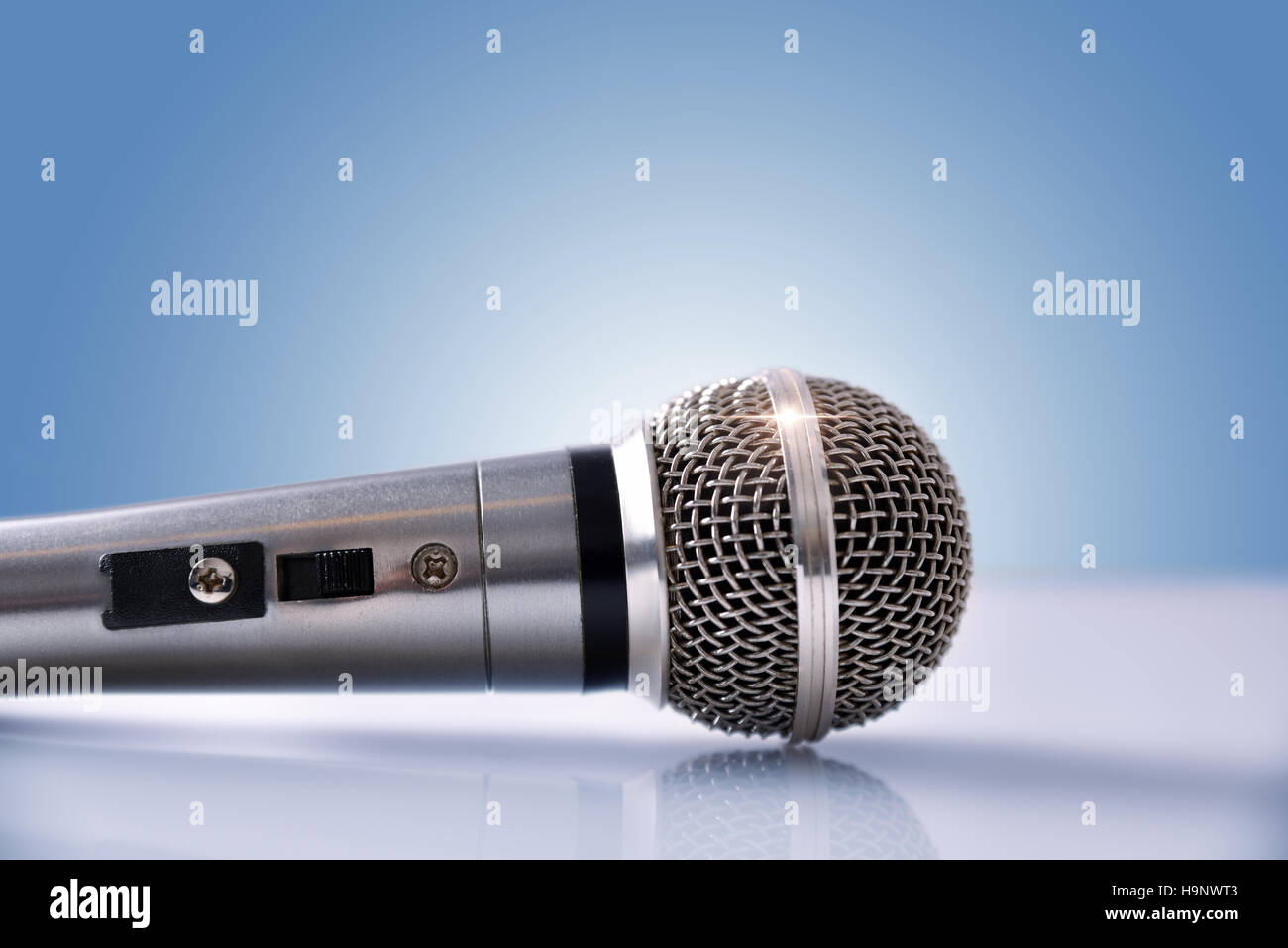 Microphone on a white glass table and blue background. Front view ...