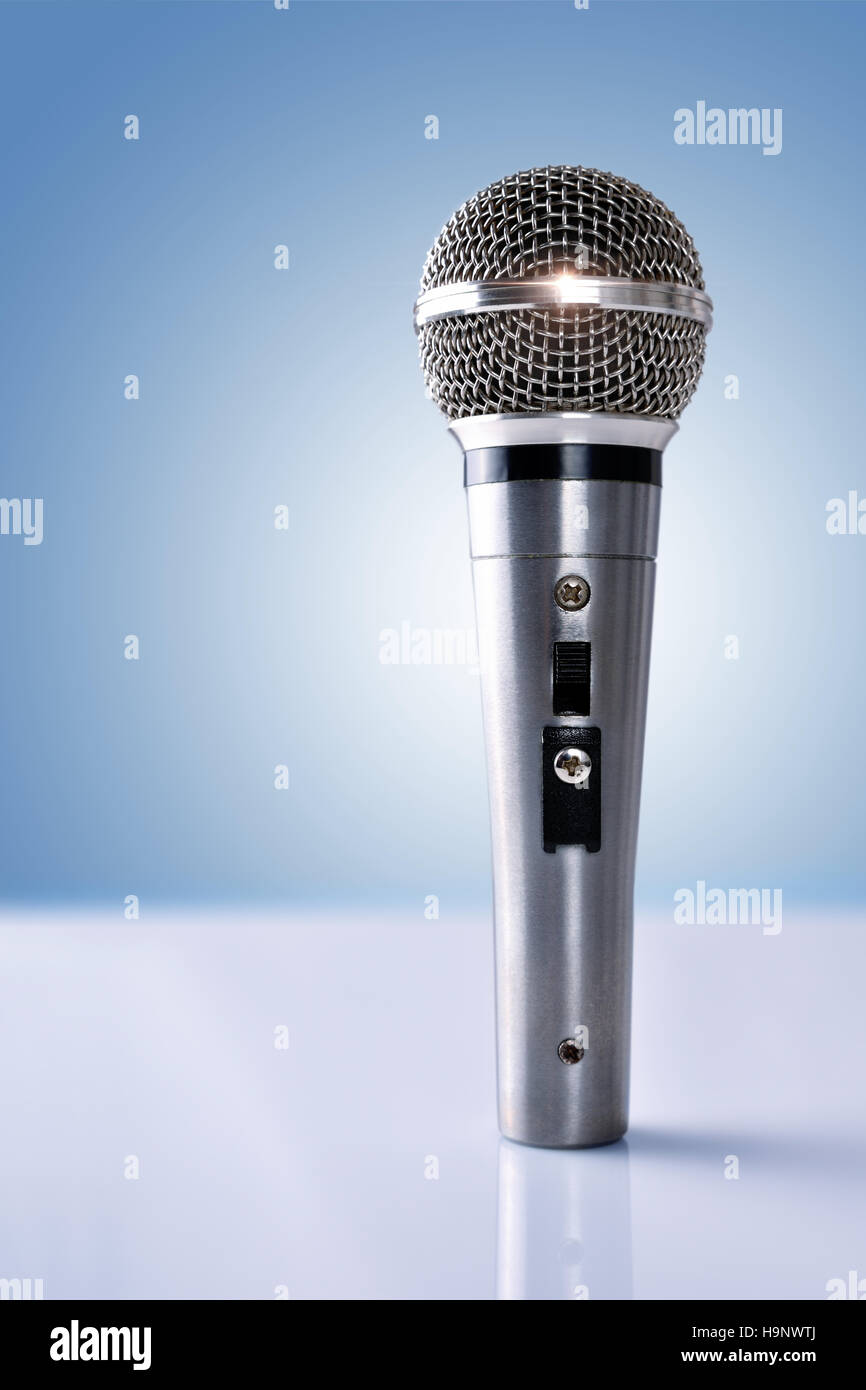 Microphone standing on a white glass table and blue background.Front ...