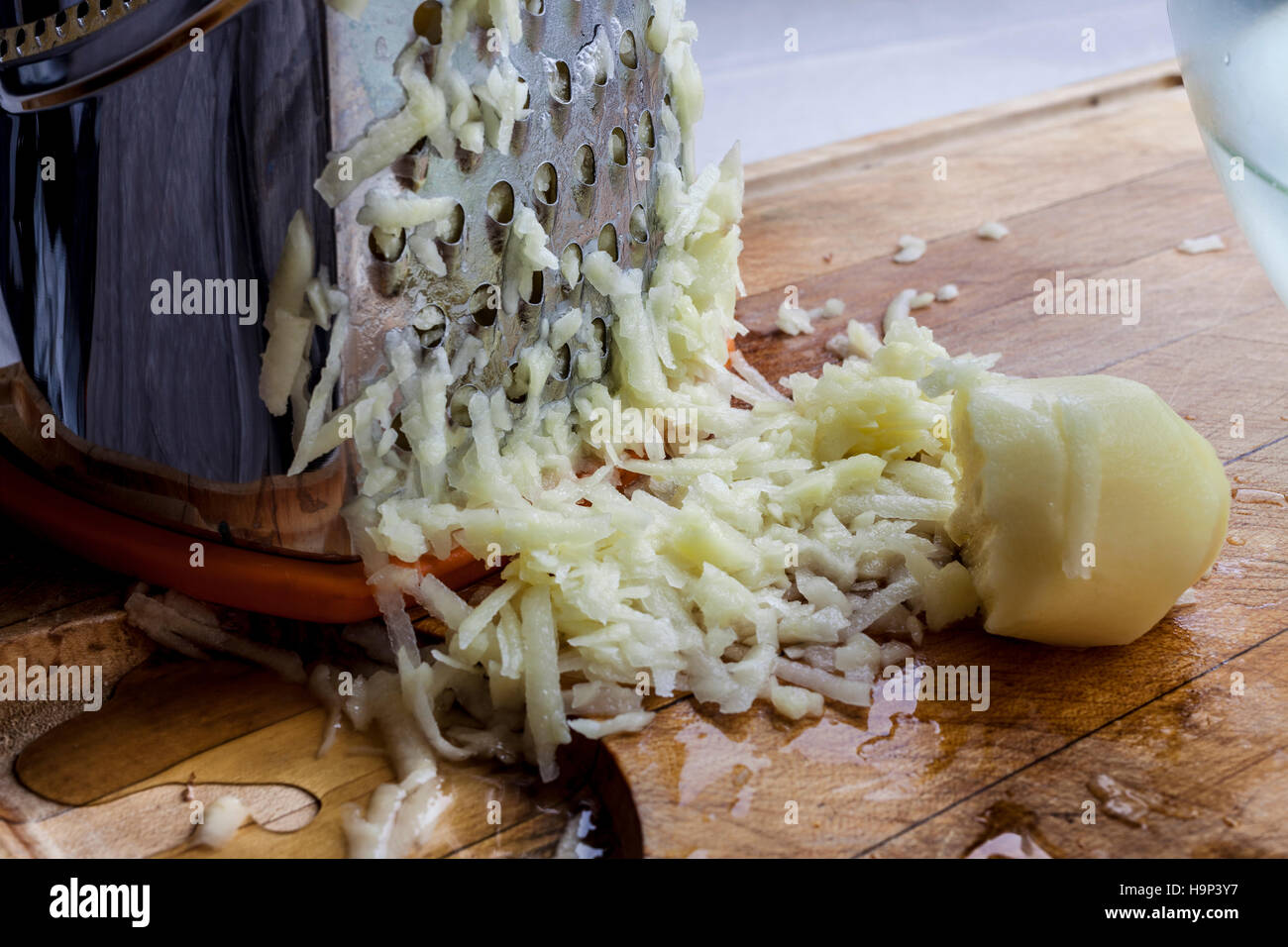 Grated potato with metal standing grater on wooden cutting board from ...
