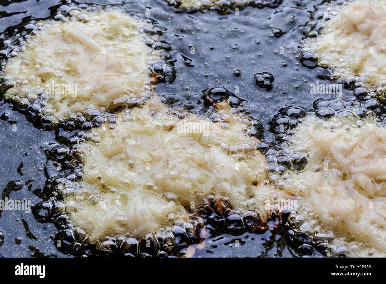 Frying latkes with raw side up in deep oil on pan from above closeup ...