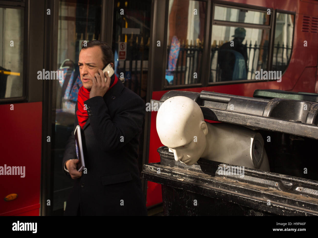 man using mobile phone as he passes head of mannequin protruding from ...