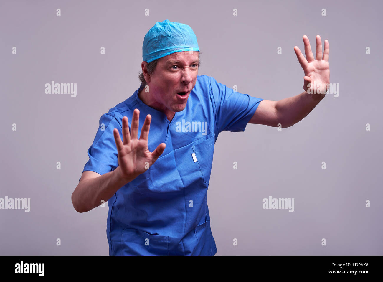 An angry middle aged male doctor standing in a blue scrubs and ...