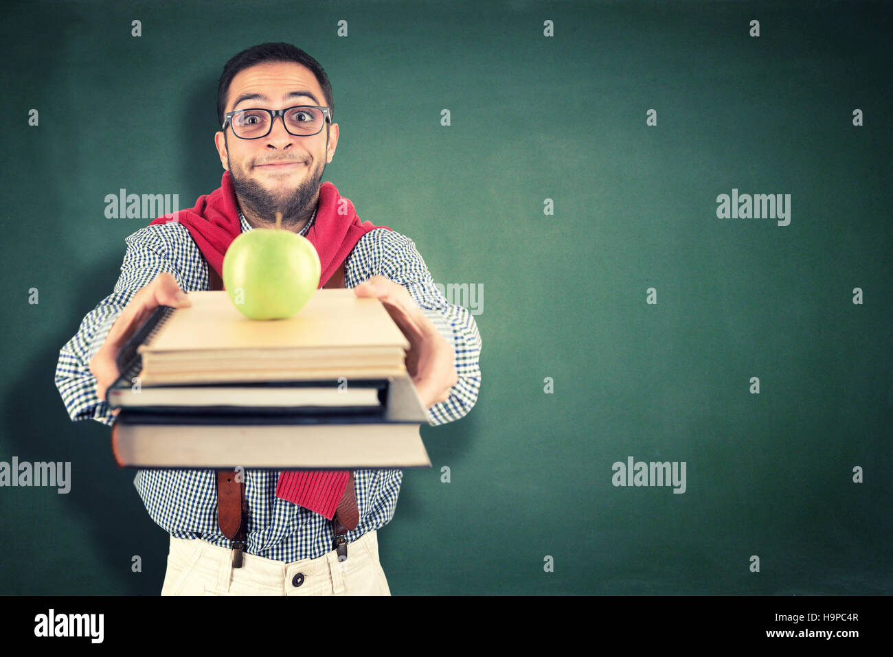 Nerd student posing with books and apple against a chalk board Stock ...