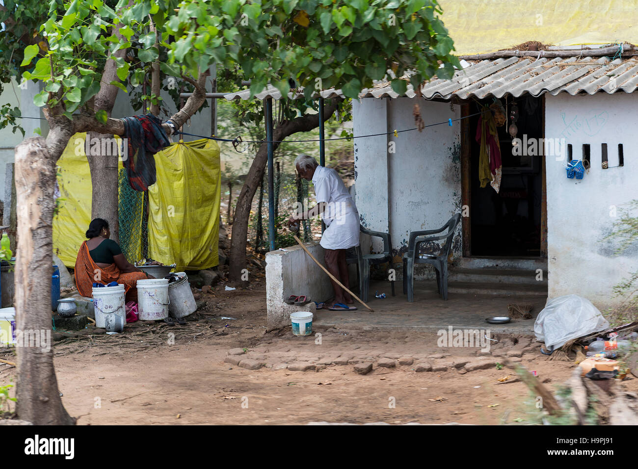 Old Indian man cleans up after cleaning his teeth whilst his wife does ...