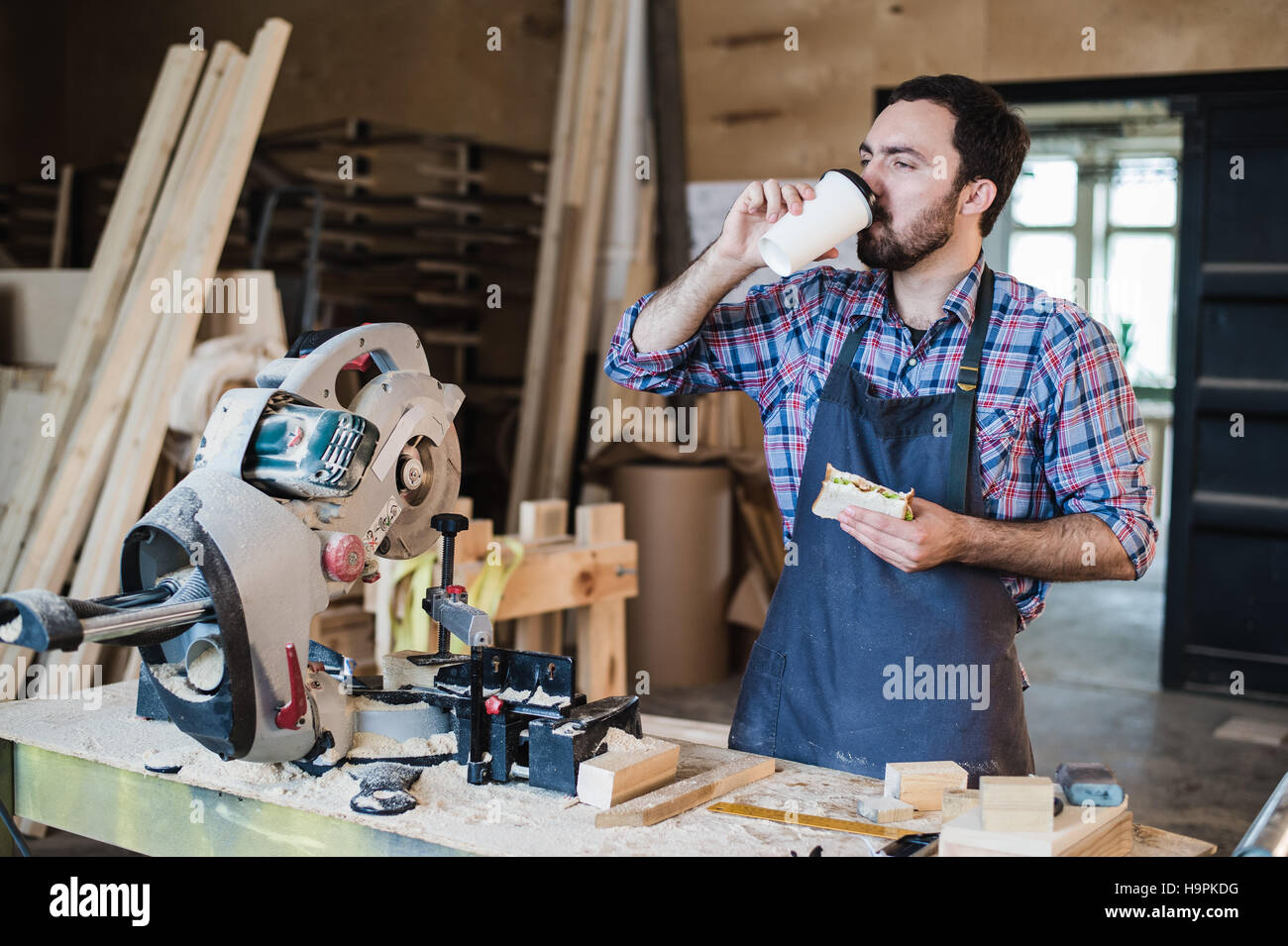 Cheerful carpentry worker having lunch eating sandwich in a workshop ...