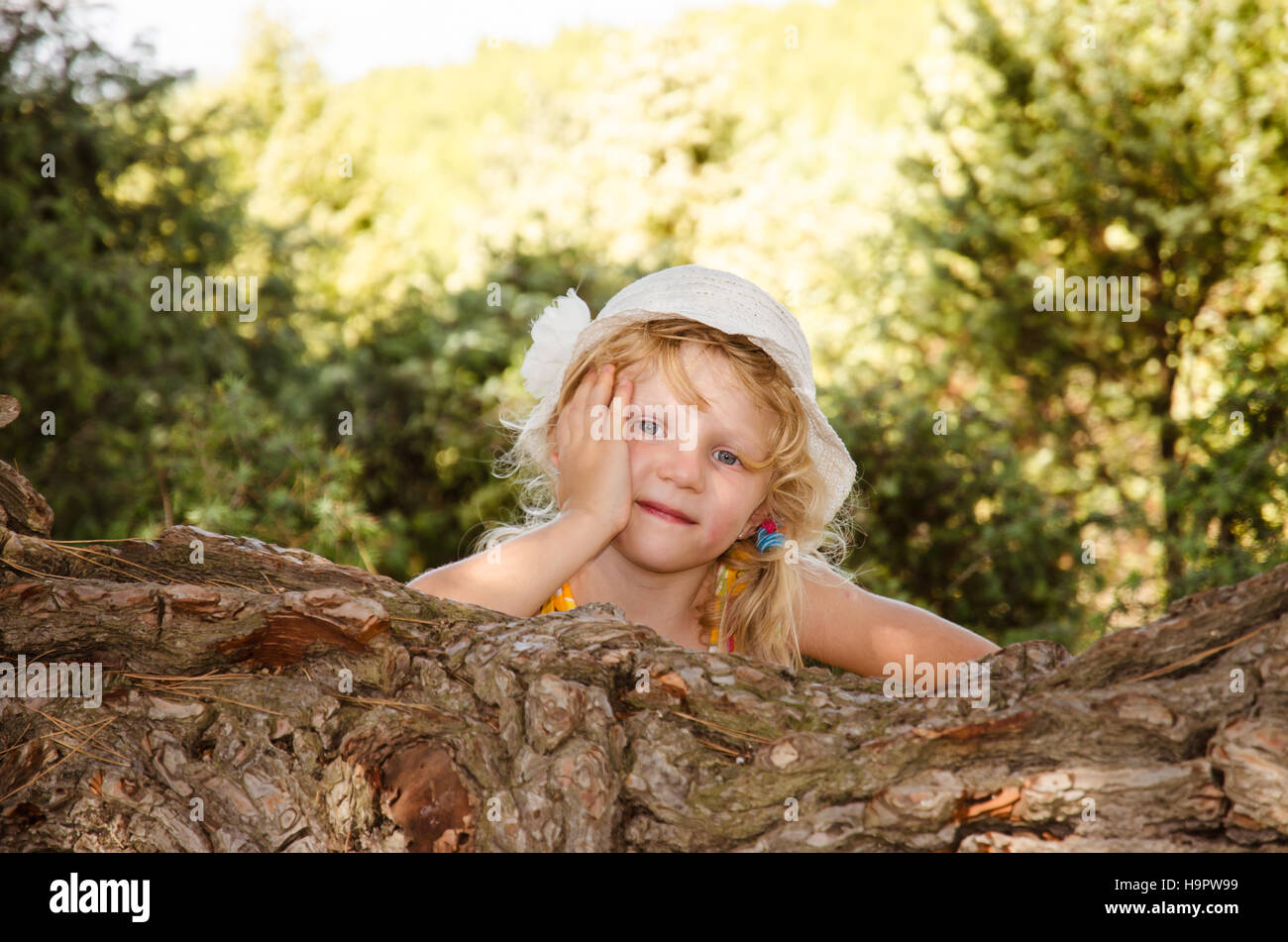 beautiful blond little girl behind tree trunk Stock Photo - Alamy